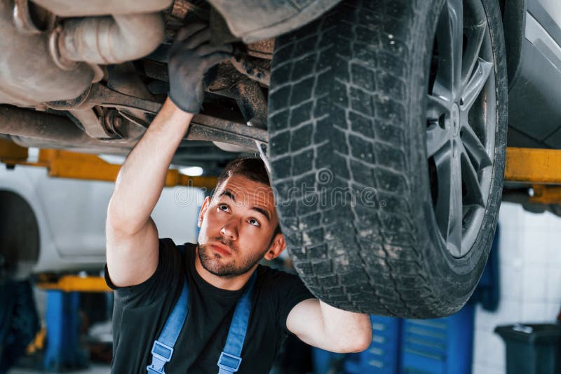 Man in Work Uniform Standing Under Car and Repairs it Indoors ...