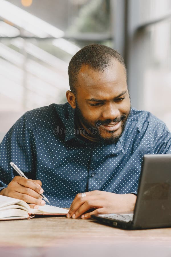 Man Working Behind A Laptop Writing In A Notebook, Cafe Stock Image ...