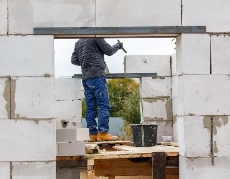 A Man is Working on a Construction Site, Laying Bricks and Using a ...