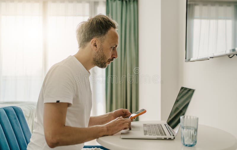Man Working from Home Using Laptop and Smartphone, Concentrating on Tasks, Representing Modern ...