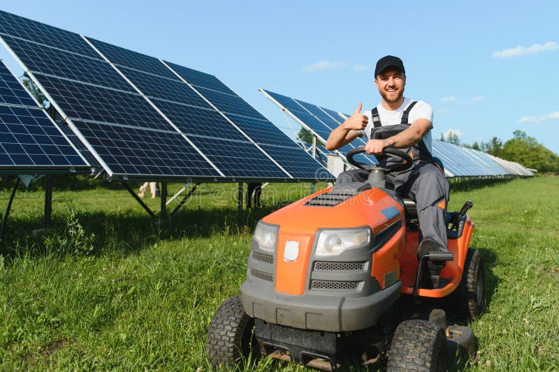 A Man Working at Solar Power Station. a Worker on a Garden Tractor Mows ...