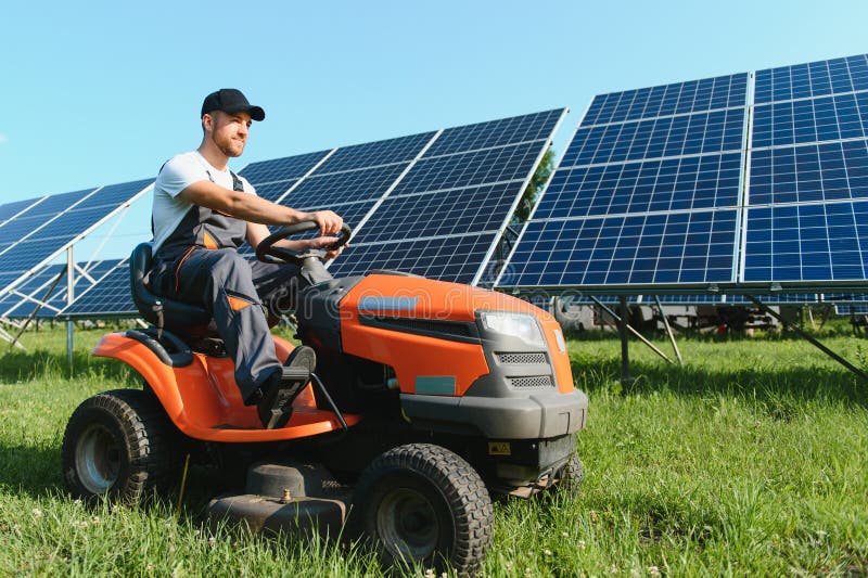 A Man Working at Solar Power Station. a Worker on a Garden Tractor Mows ...