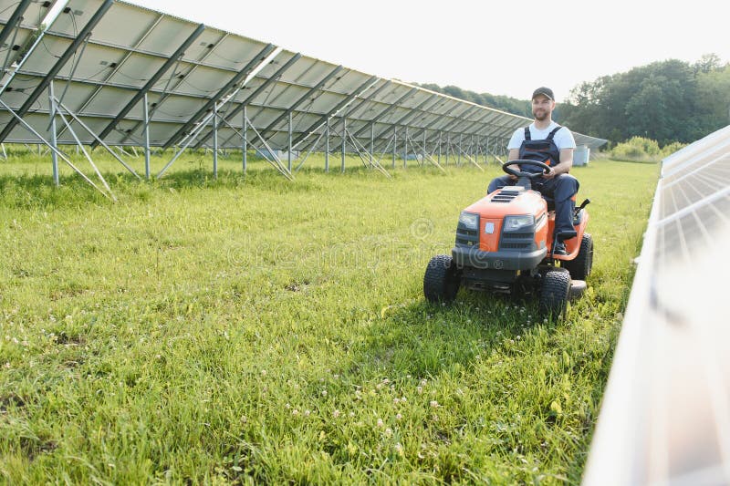 A Man Working at Solar Power Station. a Worker on a Garden Tractor Mows ...