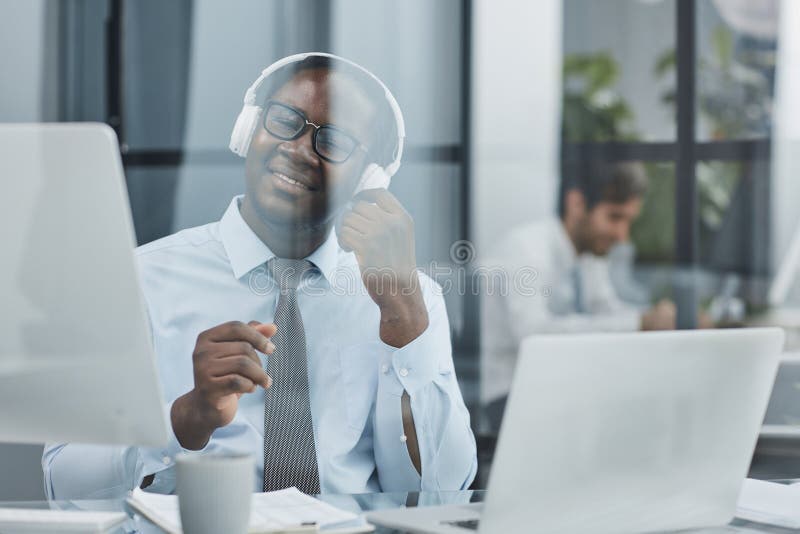 A Man at a Workplace at a Table in Front of a Computer with Headphones ...