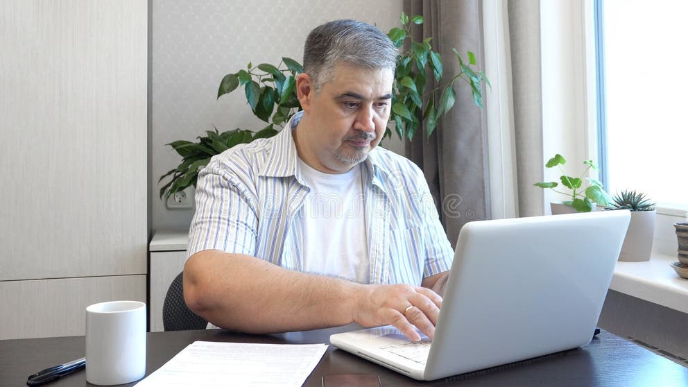 A Man Works on a Computer. he Looks at the Screen and Types on the ...