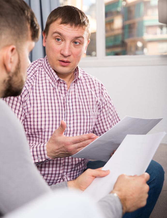 Man Worriedly Discussing Documents with Friend on Sofa at Home Stock ...