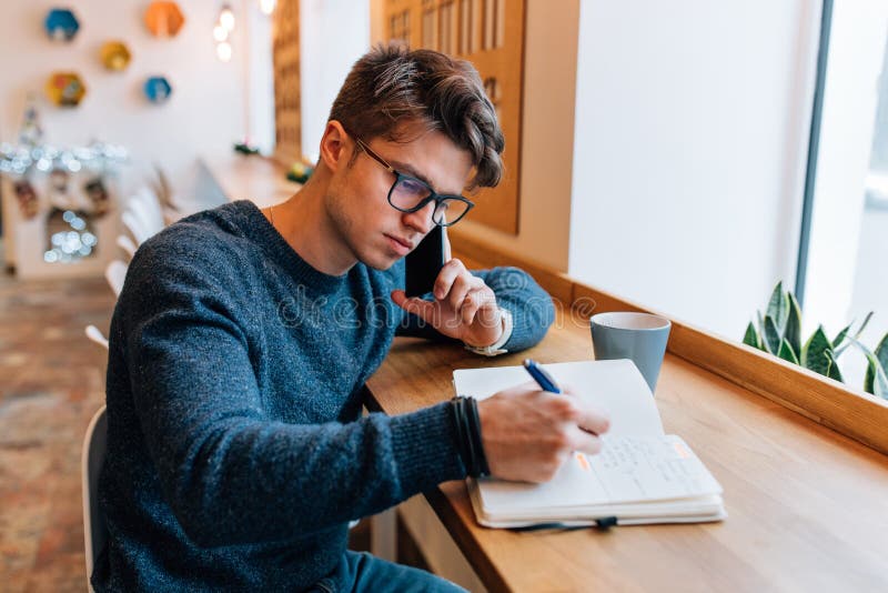 Man Writing Down Something in Notebook while Talking on Mobile Phone at ...