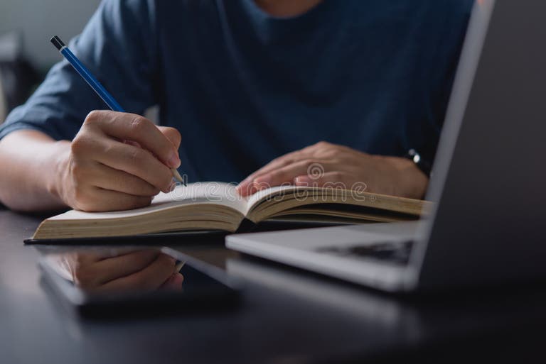 Man Writing in a Notebook while Using a Laptop, Representing Studying ...