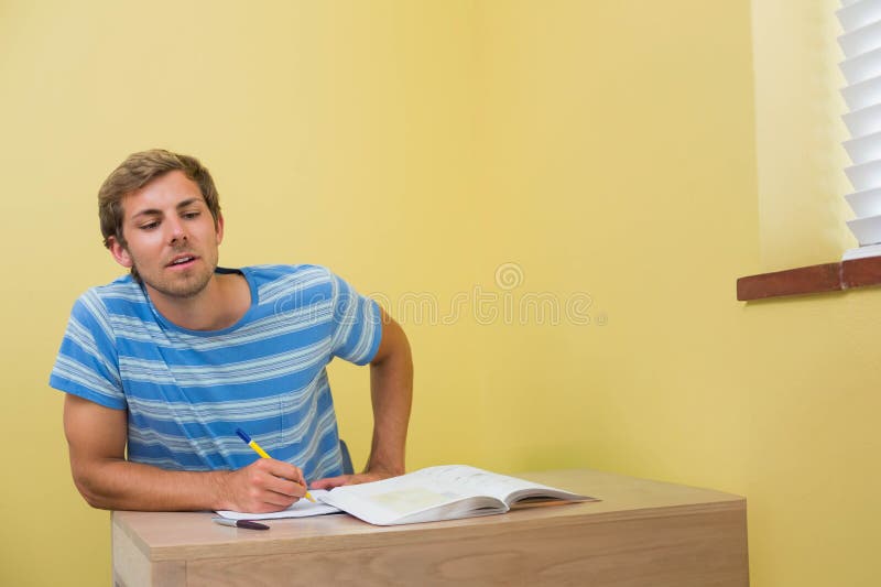 Man Writing in Open Textbook at Desk in Study Room with Pencil and Pen ...