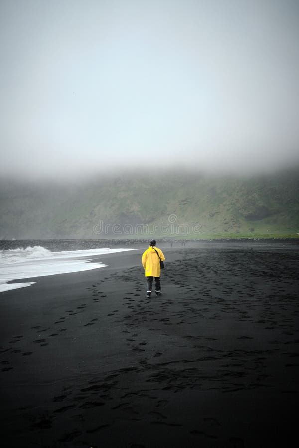 A Man Standing on a Beach Wearing a Yellow Coat and Holding a Yellow ...