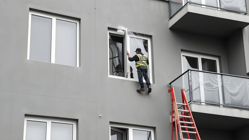 A Man in a Yellow Vest is Cleaning a Window on a Building Stock ...