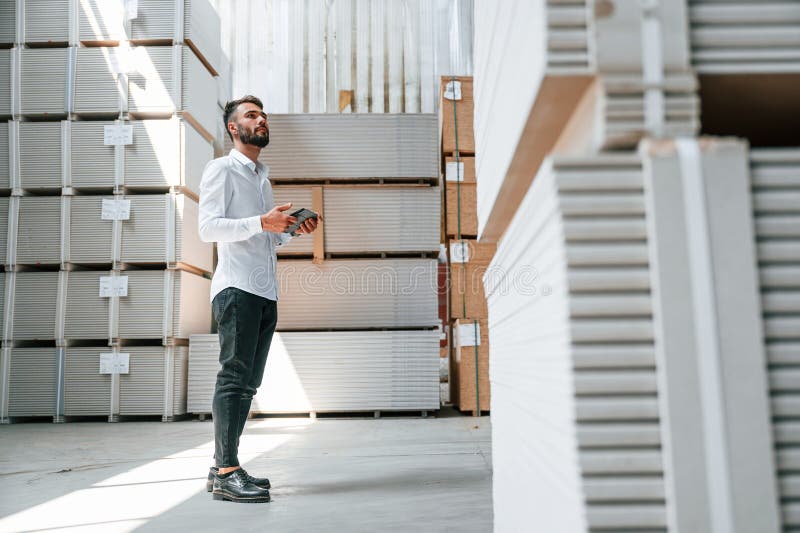 Manager Checking the Data by Using Tablet. Storage Worker is in the Warehouse with Bunch of ...