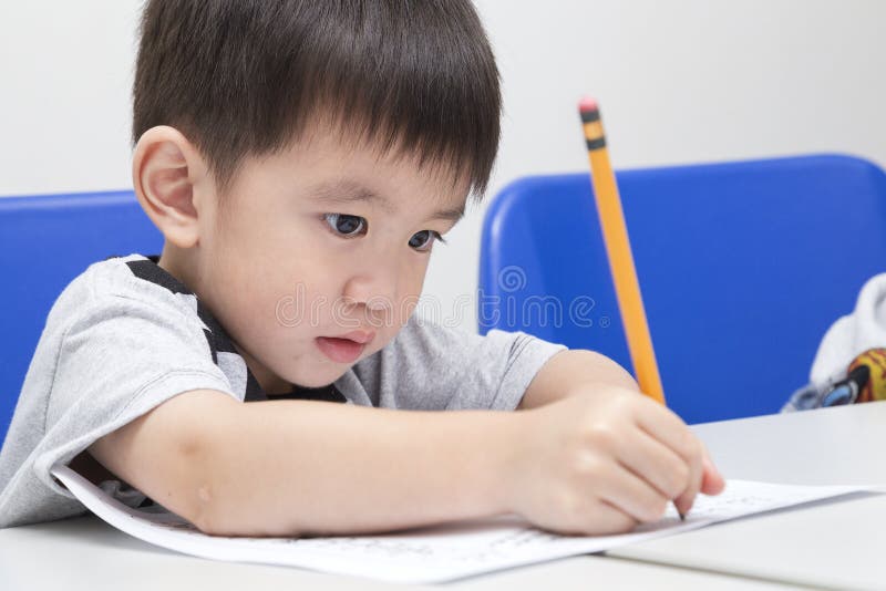 Little Boy is Learning To Write with a Pencil in Classroom at School ...