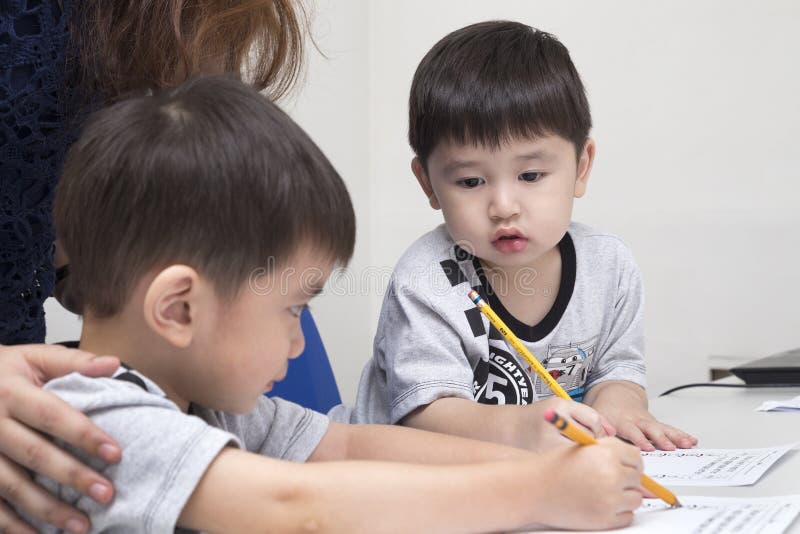 Two Little Boys Learning To Write with a Pencil in Classroom at School ...