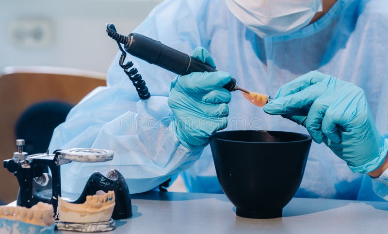 A Masked and Gloved Dental Technician Works on a Prosthetic Tooth in ...