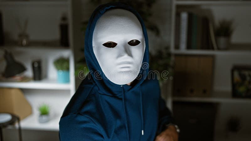 Masked Man in Hoodie Posing in a Modern Office Space, Creating a ...