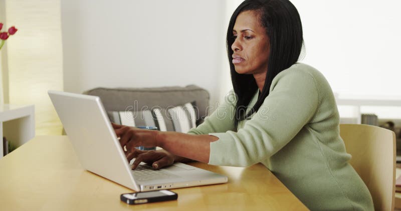 Mature African Woman Typing on Laptop Computer Looking at Screen Stock ...
