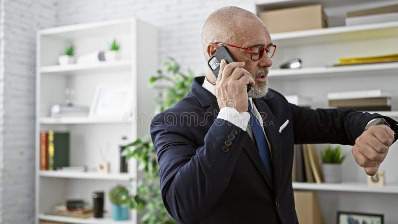 A Mature Businessman in a Suit Multitasks on a Phone Call while ...