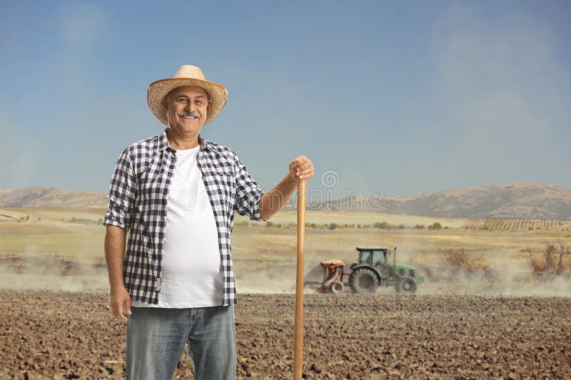 Mature Farmer with a Shovel Posing on a Field with a Tractor Stock ...