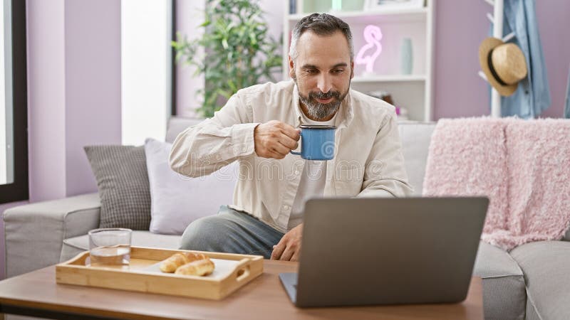 Mature Hispanic Man with Beard Using Laptop and Drinking Coffee at Home ...