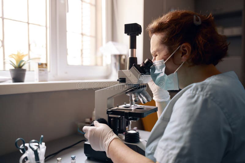 Mature Lab Assistant in Mask Looks into Microscope Researching Sample ...