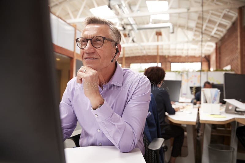 Mature Male Customer Services Agent Working At Desk In Call Center ...