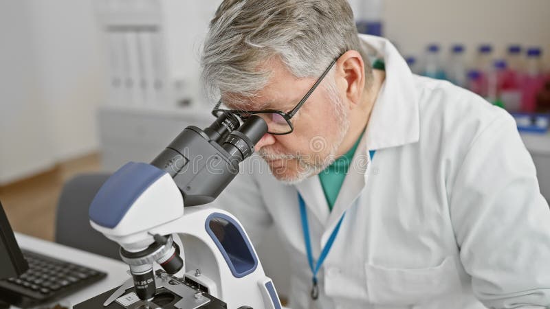 Mature Male Scientist Analyzing Samples Using a Microscope in a ...