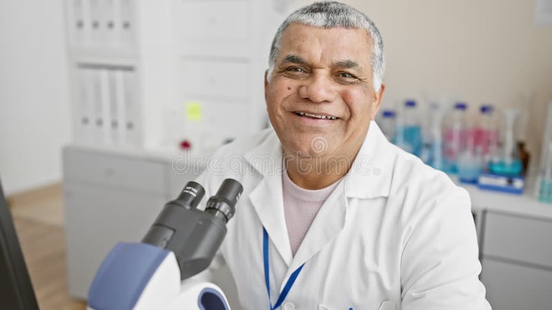 A Mature Man in a Lab Coat Smiles while Using a Microscope in a ...
