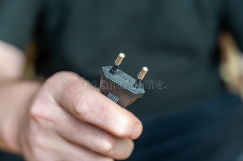 A Mature Man`s Hand is Holding an Electrical Plug. a Black Plastic AC ...