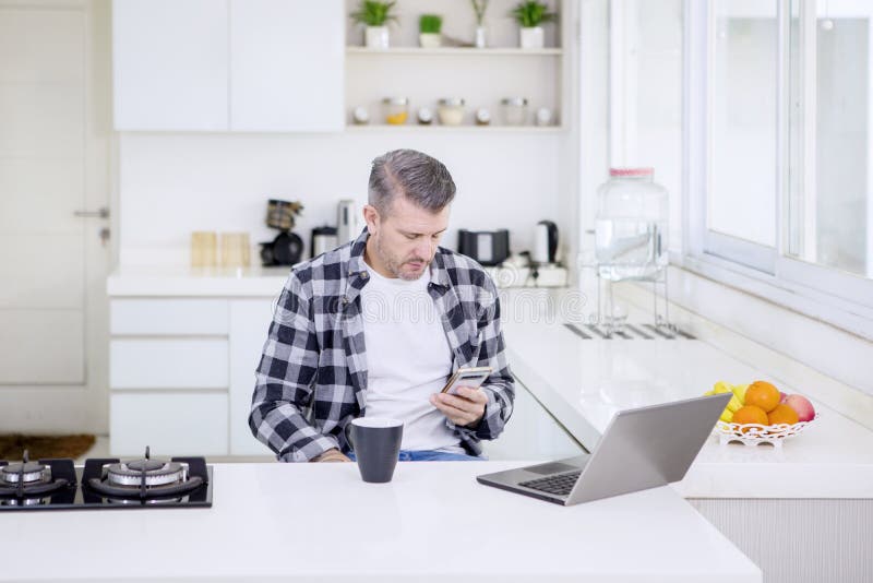 Mature Man Using Laptop and Phone in Kitchen Stock Photo - Image of ...