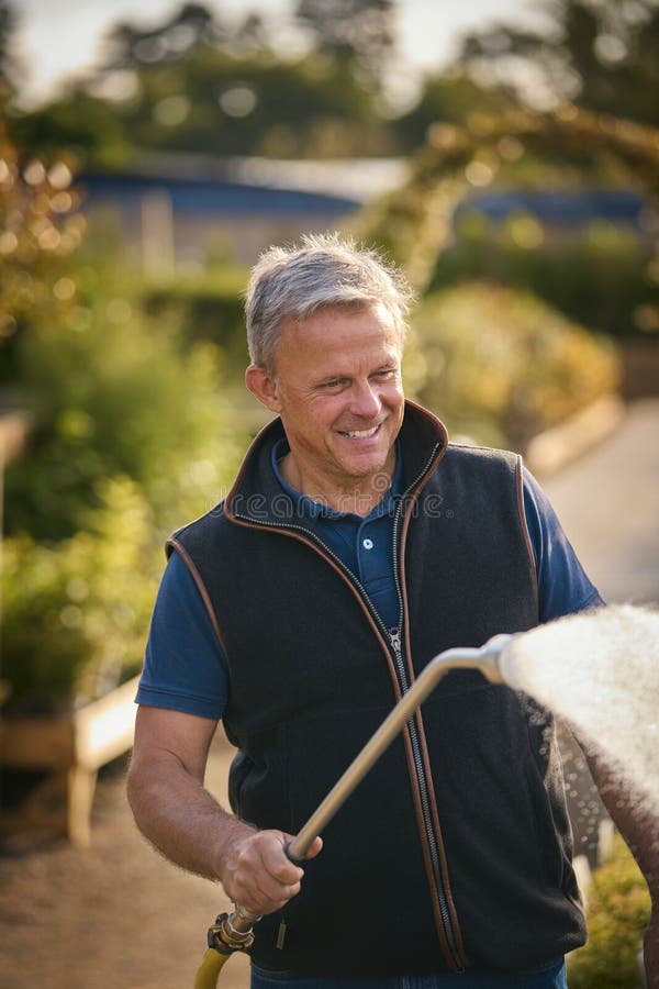 Mature Man Working Outdoors in Garden Centre Watering Plants Stock ...