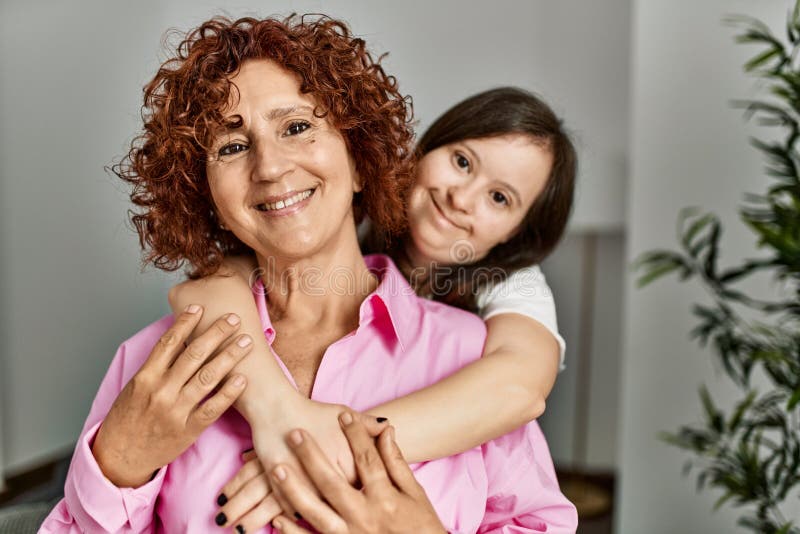 Mature Mother And Down Syndrome Daughter At Home Hugging With Love