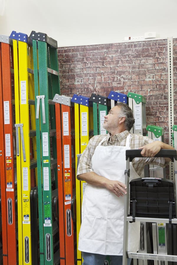 Portrait of Happy Mature Store Clerk Standing by Multicolored Ladders ...