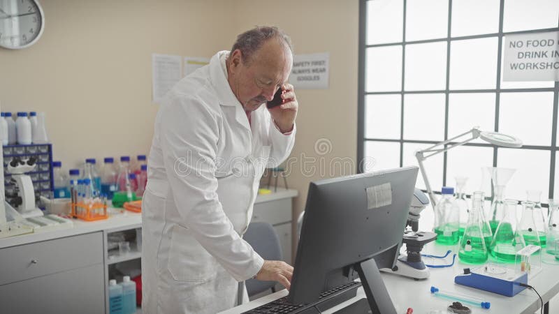 Mature Scientist in Lab Coat Using Computer and Talking on Phone in a ...