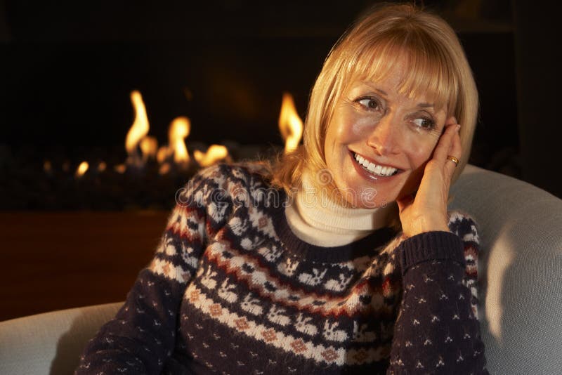 Mature Woman Relaxing in Front of Fire at Home Stock Image - Image of ...