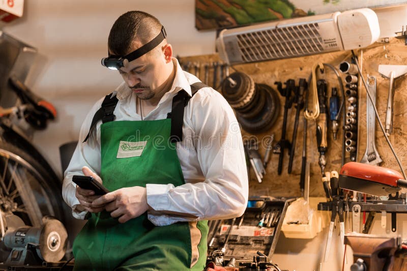 A Mechanic in a Green Apron Checking His Phone in a Workshop Stock ...