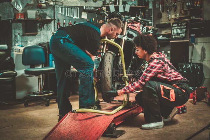 Mechanic and His Helper Repairing a Motorcycle in a Workshop Stock ...