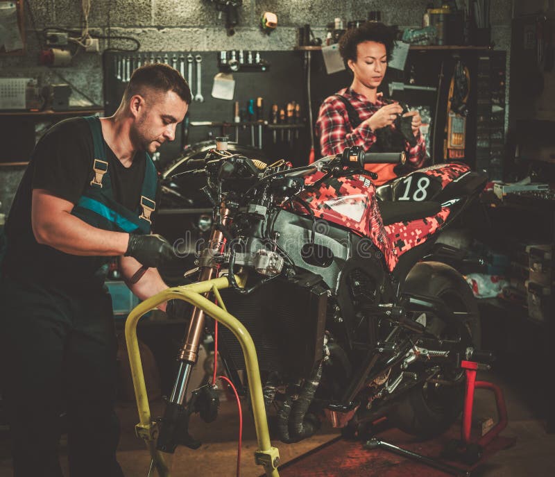 Mechanic and His Helper Repairing a Motorcycle in a Workshop Stock ...