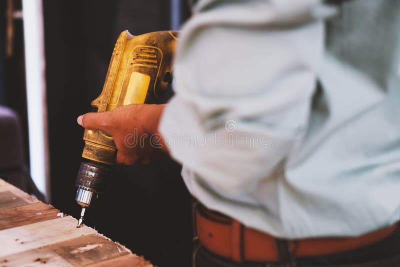 The Mechanic, the Man, is Using a Drill To Drill Wood in the ...
