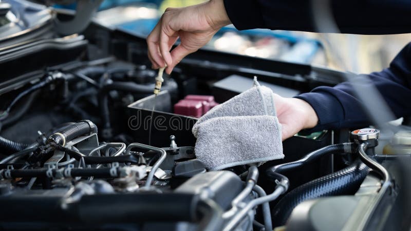 A Mechanic is Working on a Car Engine. Checking the Oil Level and Adding More Oil If Necessary ...