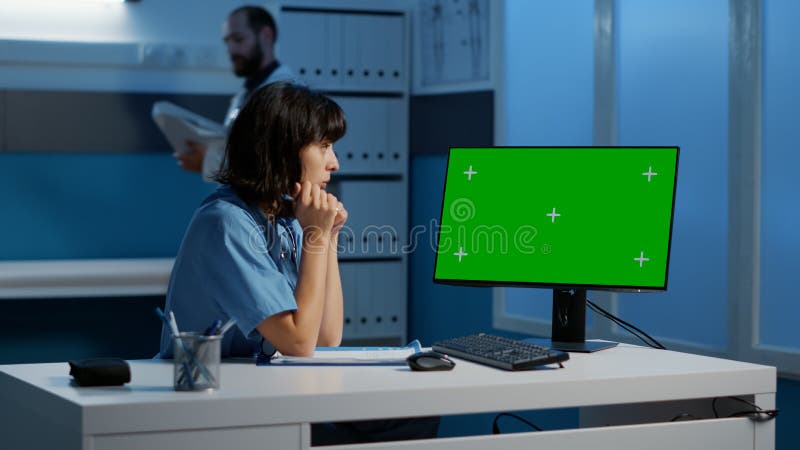 Medical Assistant Standing at Desk Looking at Computer with Green ...