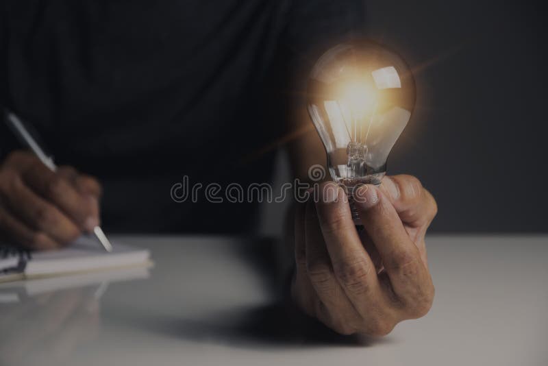 Men Holding Light Bulb on the Desk in Office and Writing on Note Book ...