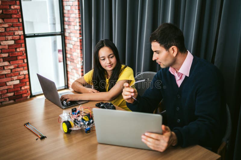 Mentor and Student Collaborate on Robot Development in Modern Workspace. Robotics Project Blends ...