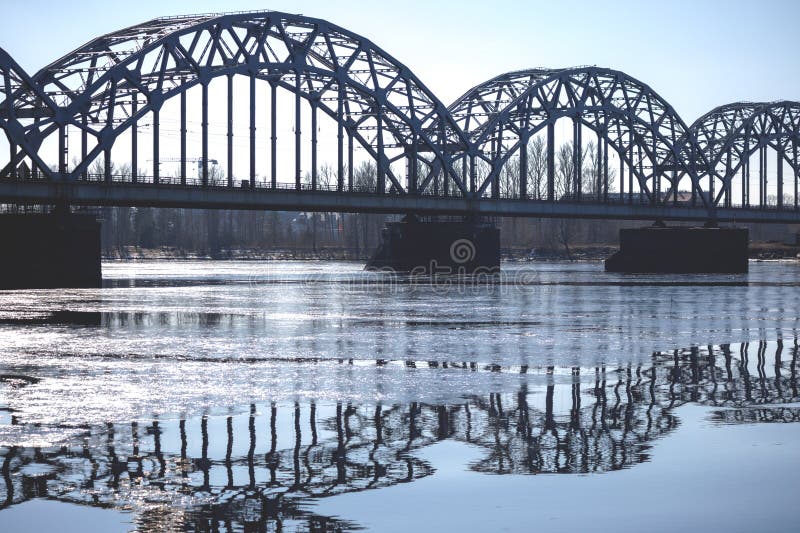 A Metal Arched Bridge Over a Blue River with the Reflection of the ...