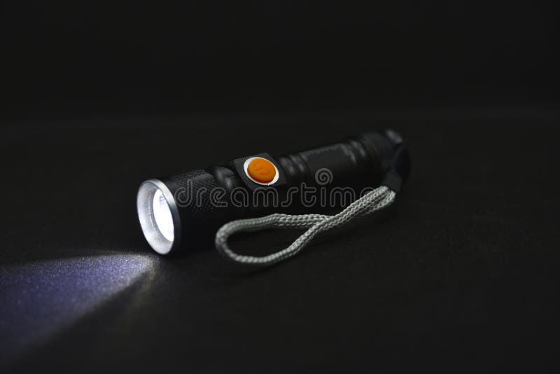 Metal Black Flashlight on a Black Background. Burning Pocket Flashlight ...