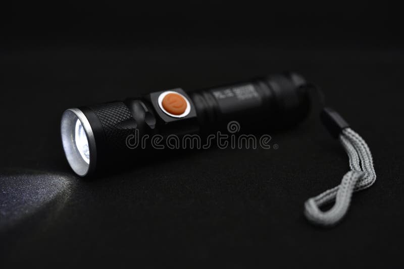 Metal Black Flashlight on a Black Background. Burning Pocket Flashlight ...