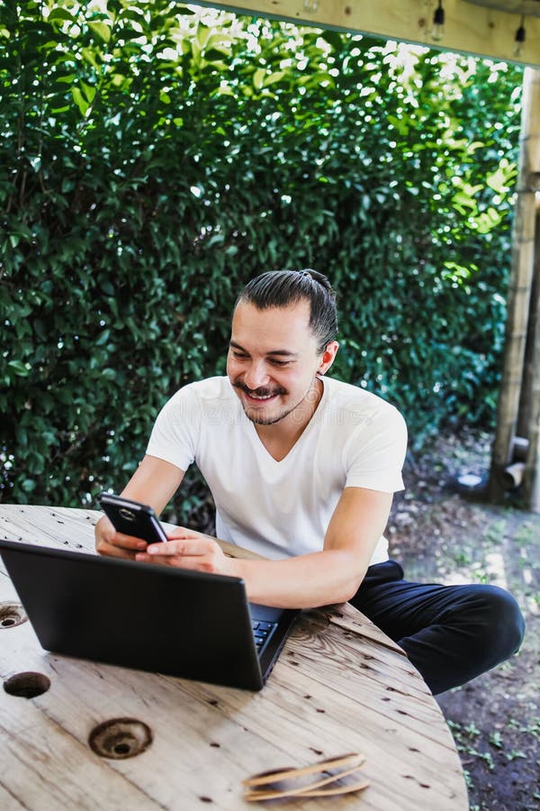 Mexican Man Using a Smartphone and Computer in a Home Terrace in Mexico ...