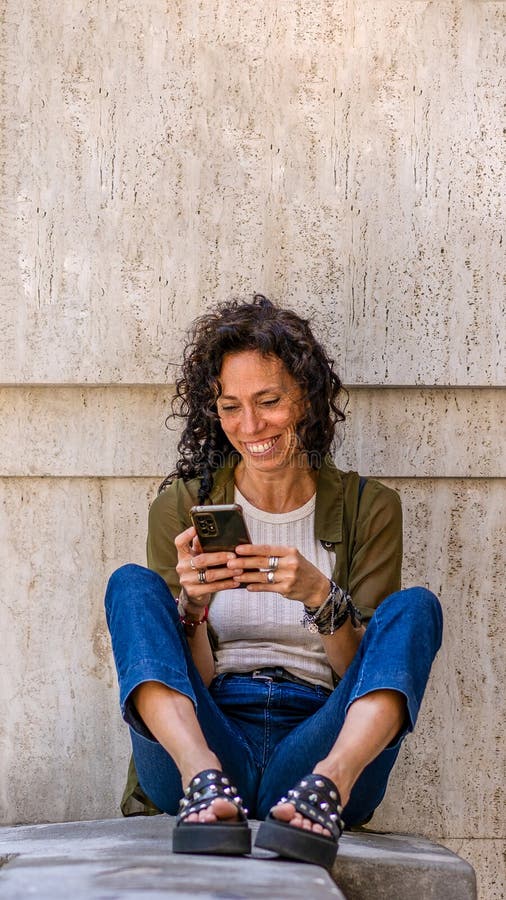 Mid-adult Woman Sitting on a Ledge while Using Her Smartphone Stock ...