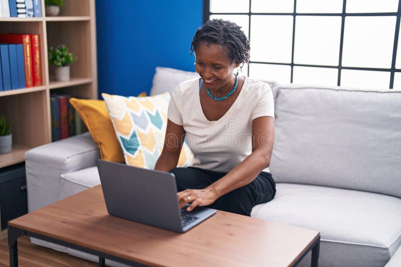 Middle Age African American Woman Using Laptop Sitting On Sofa At Home