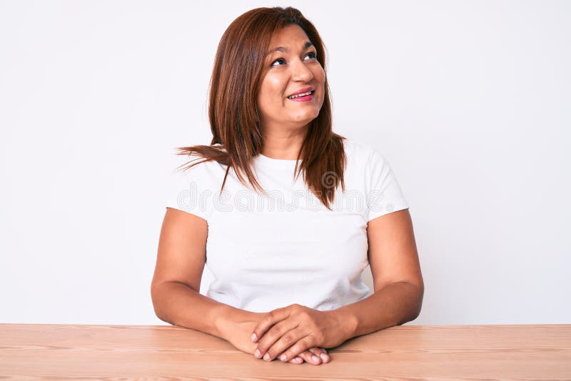 Middle Age Brunette Hispanic Woman Wearing Casual White Tshirt Sitting